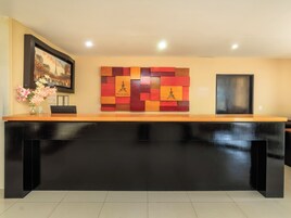 Uma receção com balcão preto, um quadro emoldurado com vista urbana, uma obra de arte abstrata colorida e um vaso com flores.