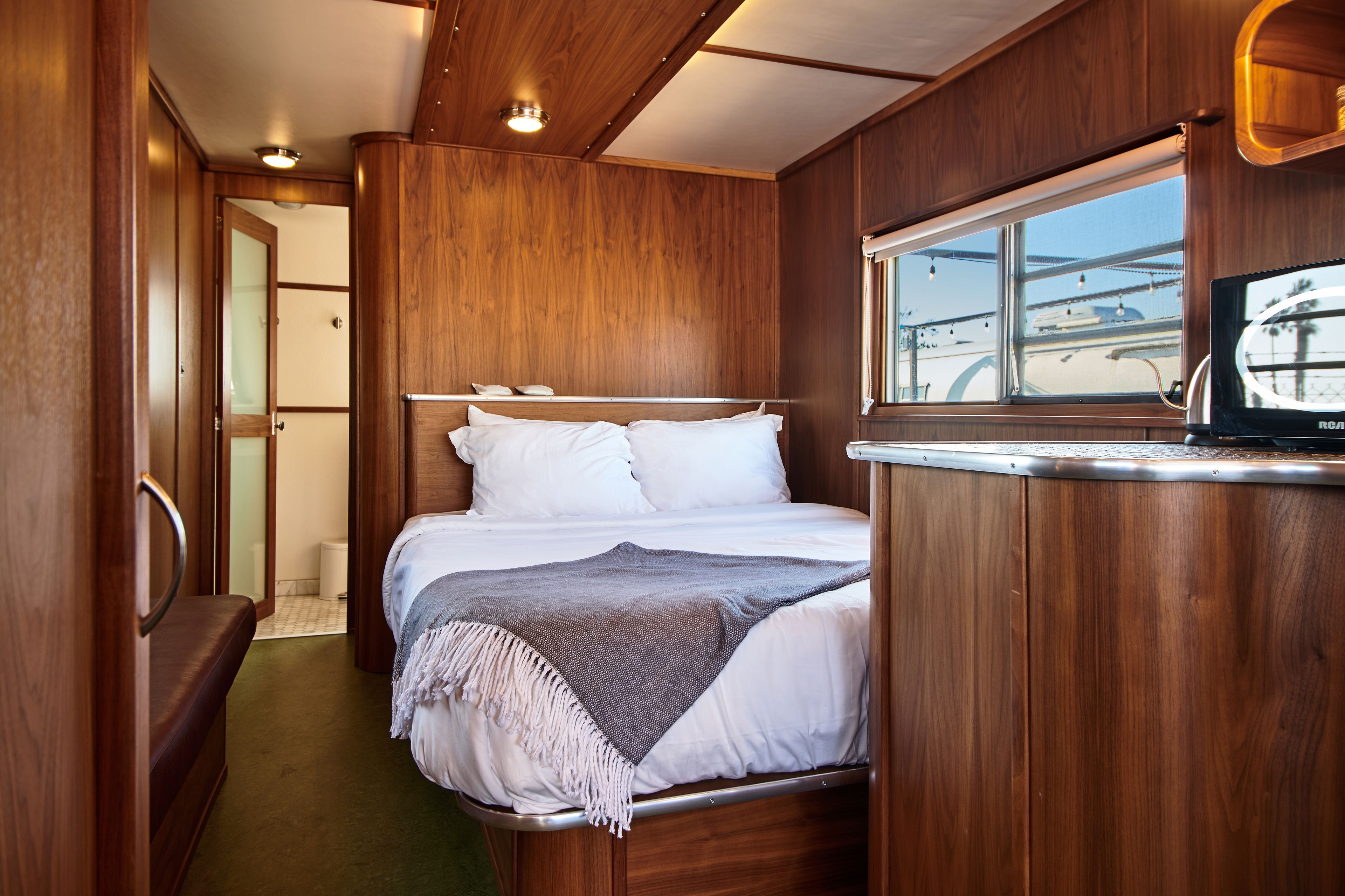 Quarto com painéis de madeira, uma cama, um banco e uma janela com vista para o exterior.