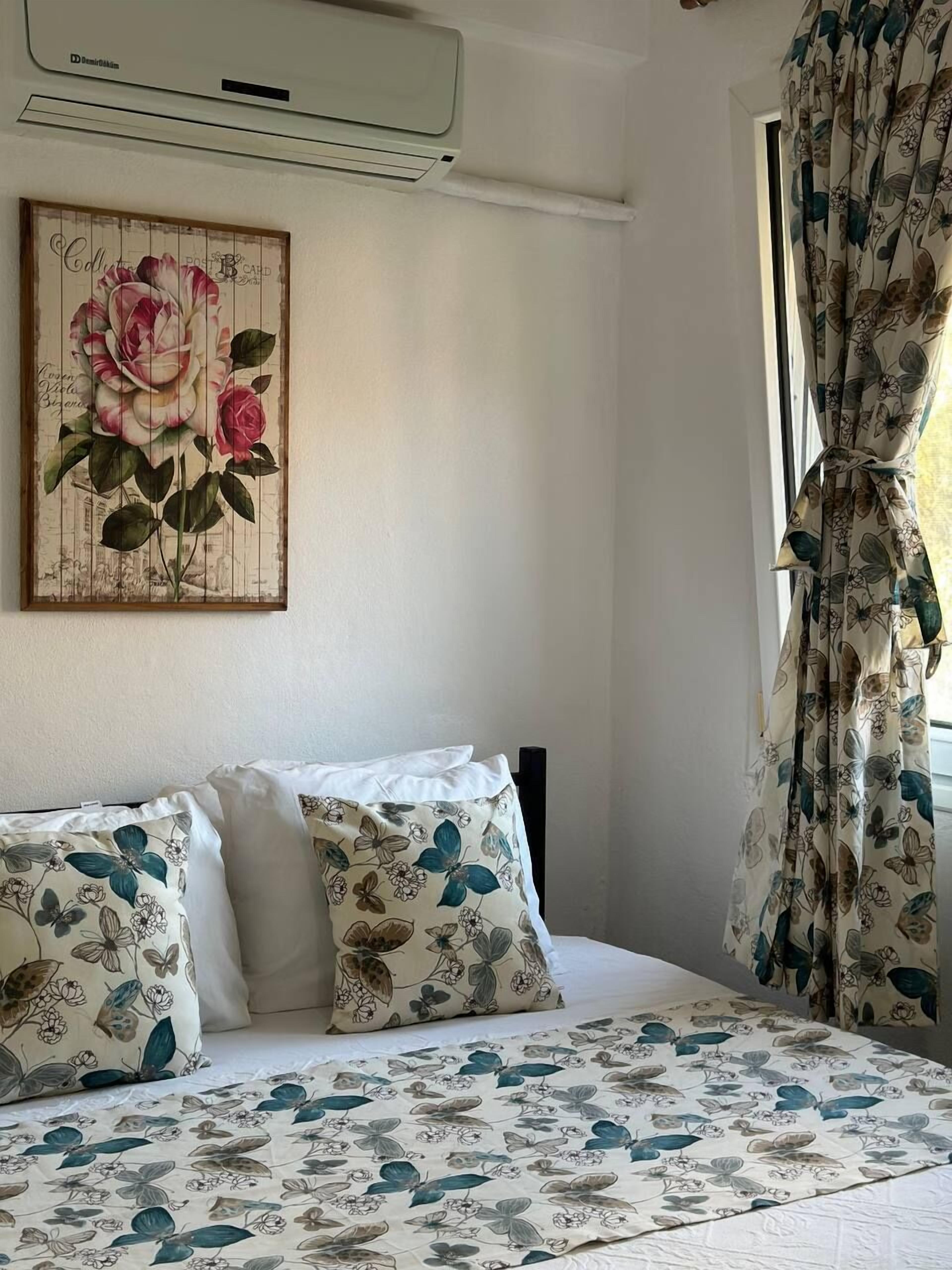 Quarto com colcha florida, almofadas a combinar e cortina estampada.