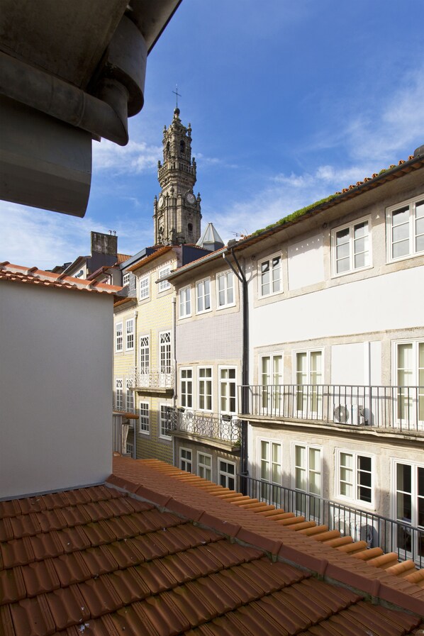 Vista de um edifício com torre de relógio, telhado em azulejos e varanda com grade.