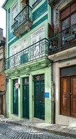 Um edifício verde com varanda, duas portas verdes e uma porta de madeira.