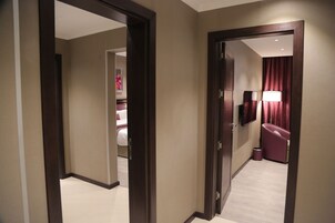 Corredor de hotel com espelho, lixeira e área de estar com abajur.