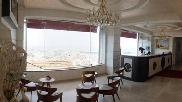 Um saguão de hotel com uma grande janela que oferece vista para a cidade, uma recepção e um candelabro.