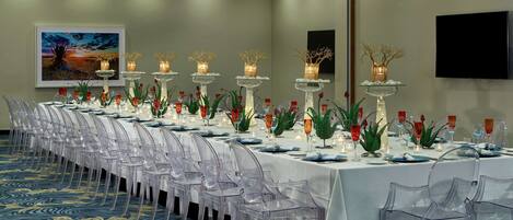 Uma longa mesa de jantar posta com cadeiras transparentes, velas e vasos decorativos.