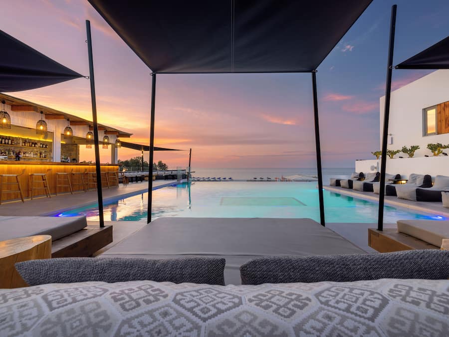 Área de piscina com bar, espreguiçadeiras e vista para o mar ao pôr do sol.