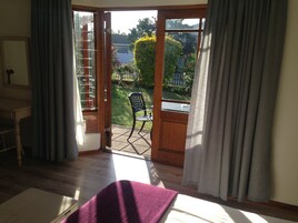 Quarto com uma cama, uma mesa e vista para um jardim através de uma porta aberta.