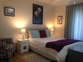 Quarto com cama, duas mesas de cabeceira, um criado-mudo, uma poltrona estampada e um tapete.