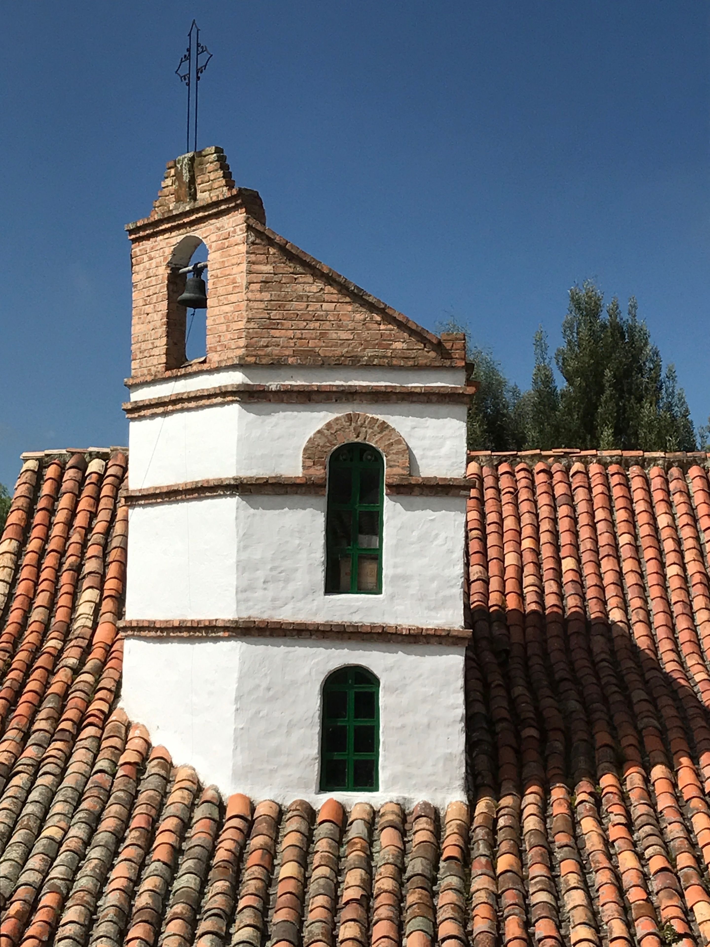 Um edifício com uma torre de sino, uma pequena janela em arco e uma porta verde.