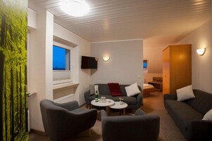 Uma sala de estar moderna com sofá, duas poltronas, mesa de centro e televisão de tela plana fixada na parede.