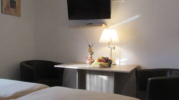Quarto de hotel com duas camas, uma escrivaninha com luminária, televisão de tela plana e uma cesta de frutas.