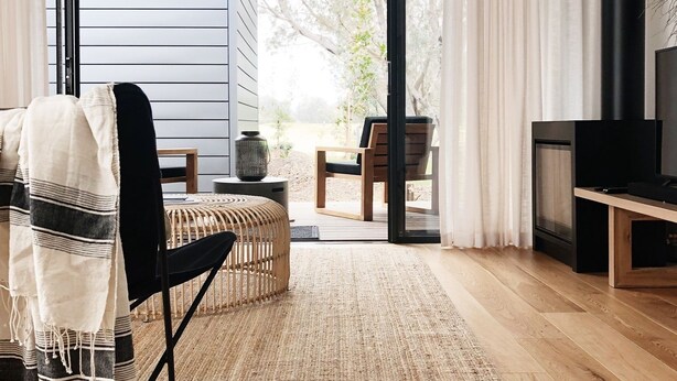 Uma sala de estar moderna com uma ampla porta de vidro deslizante que dá para uma área externa, piso de madeira e um sofá preto.
