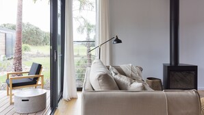 Uma sala de estar moderna com um sofá, um banquinho redondo, um abajur preto e uma lareira a lenha de madeira preta.