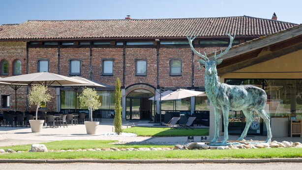 Um edifício com fachada de tijolos, área de estar ao ar livre com guarda-sóis e uma grande estátua de veado.