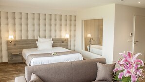 Quarto de hotel com uma cama grande, um sofá, um espelho e um vaso de planta.