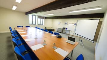 Uma sala de conferências com uma mesa comprida, cadeiras azuis, um quadro branco e um laptop.