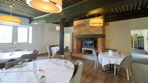 Restaurante com mesas redondas, cadeiras e uma lareira de tijolos.