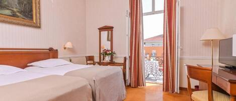 Quarto de hotel com duas camas, uma escrivaninha, uma cadeira, televisão e varanda com vista para edifícios.
