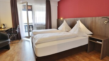 Quarto de hotel com cama, mesas de cabeceira, uma cadeira e vista para o exterior.