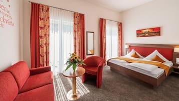 Quarto de hotel com uma cama, uma poltrona vermelha, uma mesinha com um vaso de flores e um quadro na parede.