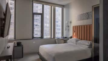 Quarto de hotel moderno com uma cama grande, uma escrivaninha, uma cadeira e uma janela com vista para a cidade.
