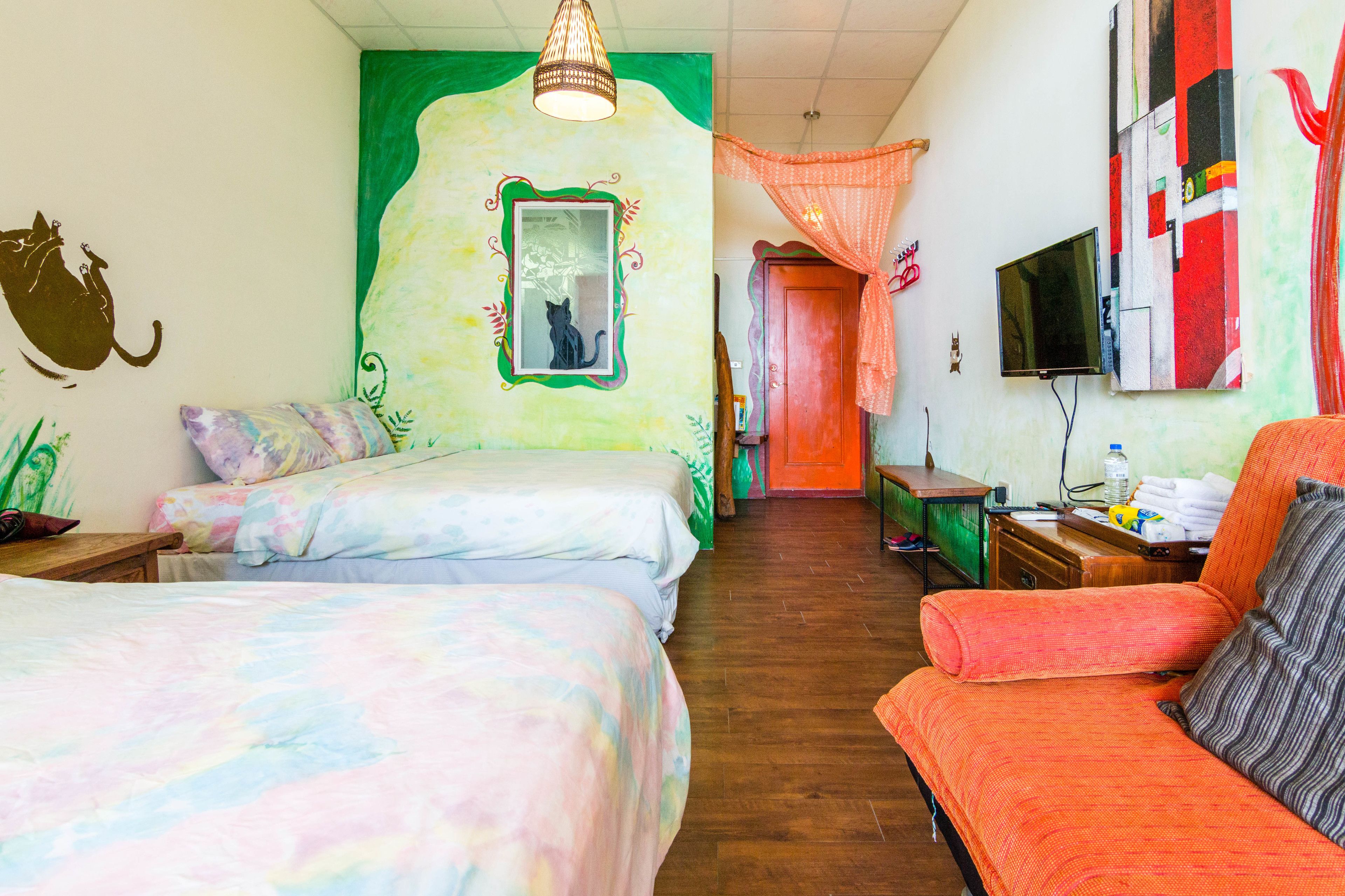 Quarto de hotel com duas camas, uma televisão, uma escrivaninha e um mural colorido na parede.