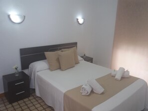 Quarto de hotel com uma cama, duas mesas de cabeceira e uma luminária fixada na parede.