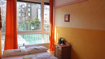 Quarto de hotel com uma cama, mesa de cabeceira, abajur e janela com cortinas.