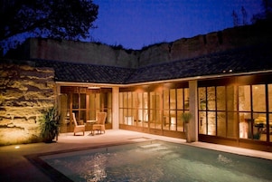 Área de piscina com muro de pedra, piscina e espaço de estar com cadeiras e mesa.