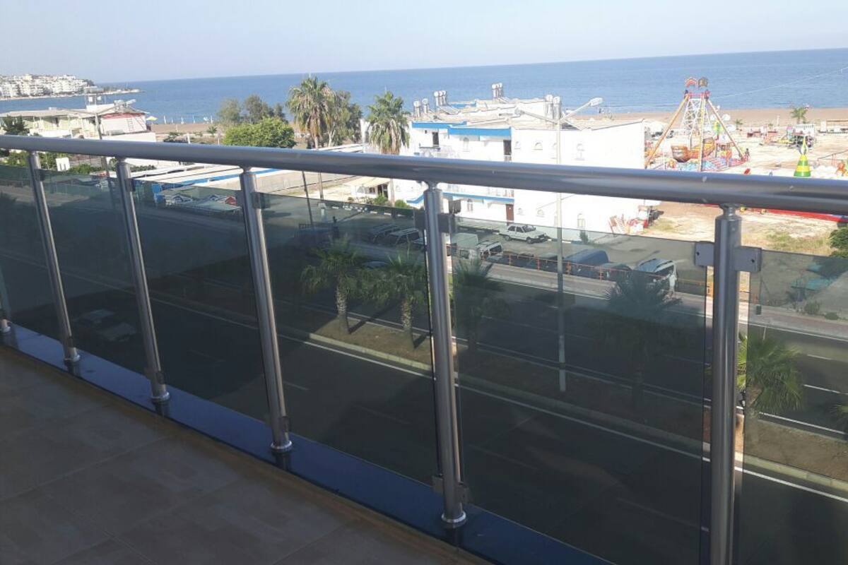 Uma varanda com vista para uma praia, um parque de estacionamento e um edifício com telhado azul.