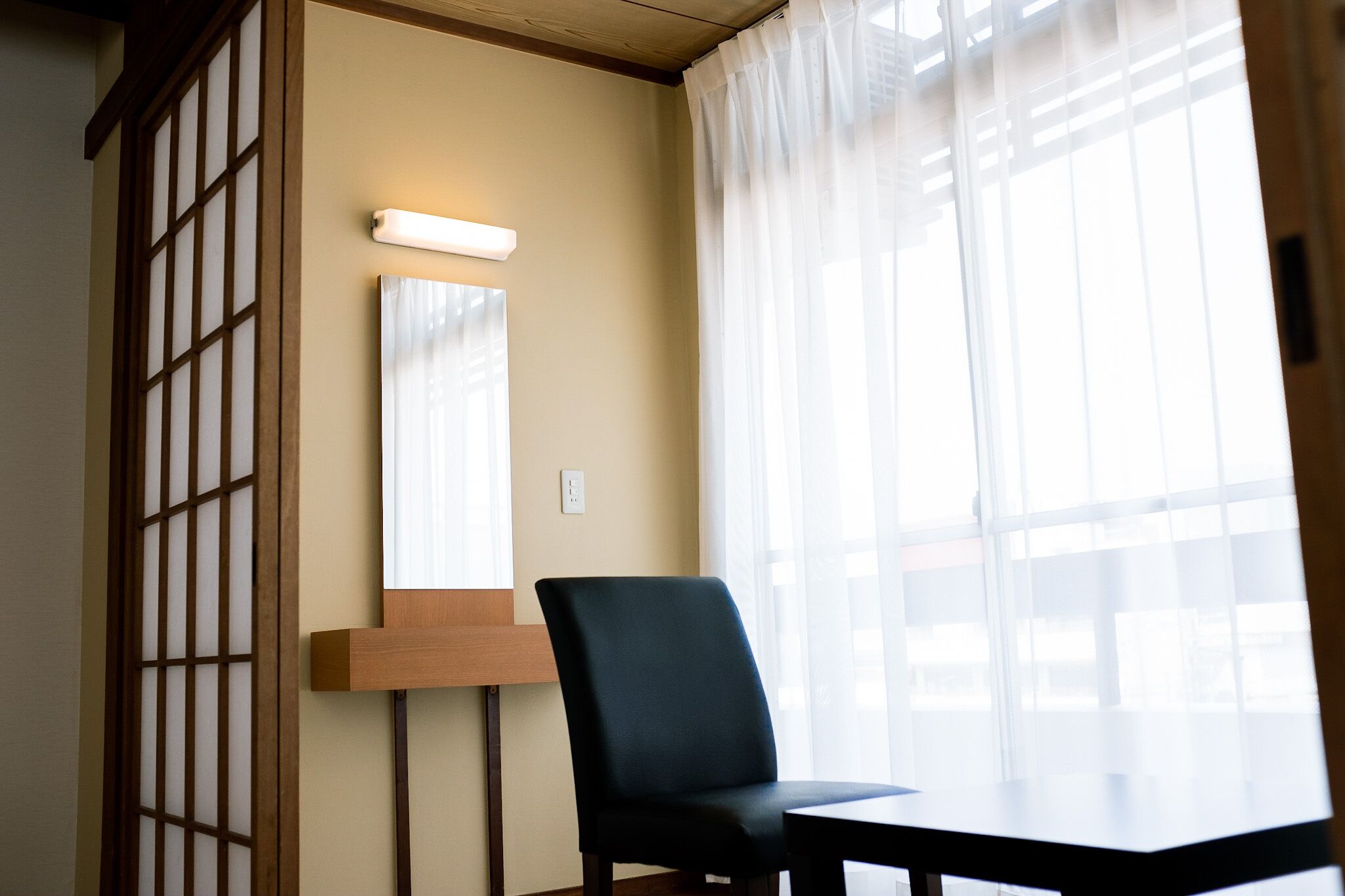 Um quarto com uma porta japonesa tradicional deslizante, uma cadeira preta, uma mesinha e um aplique de parede.