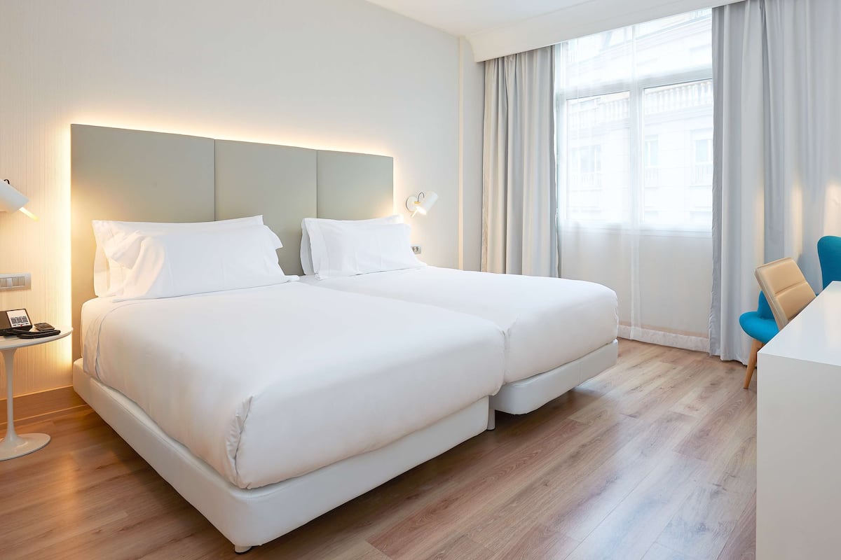 Quarto de hotel com uma cama de casal, mesas de cabeceira, escrivaninha e uma cadeira.