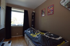 Quarto com cama, janela, estante de livros e duas imagens emolduradas na parede.