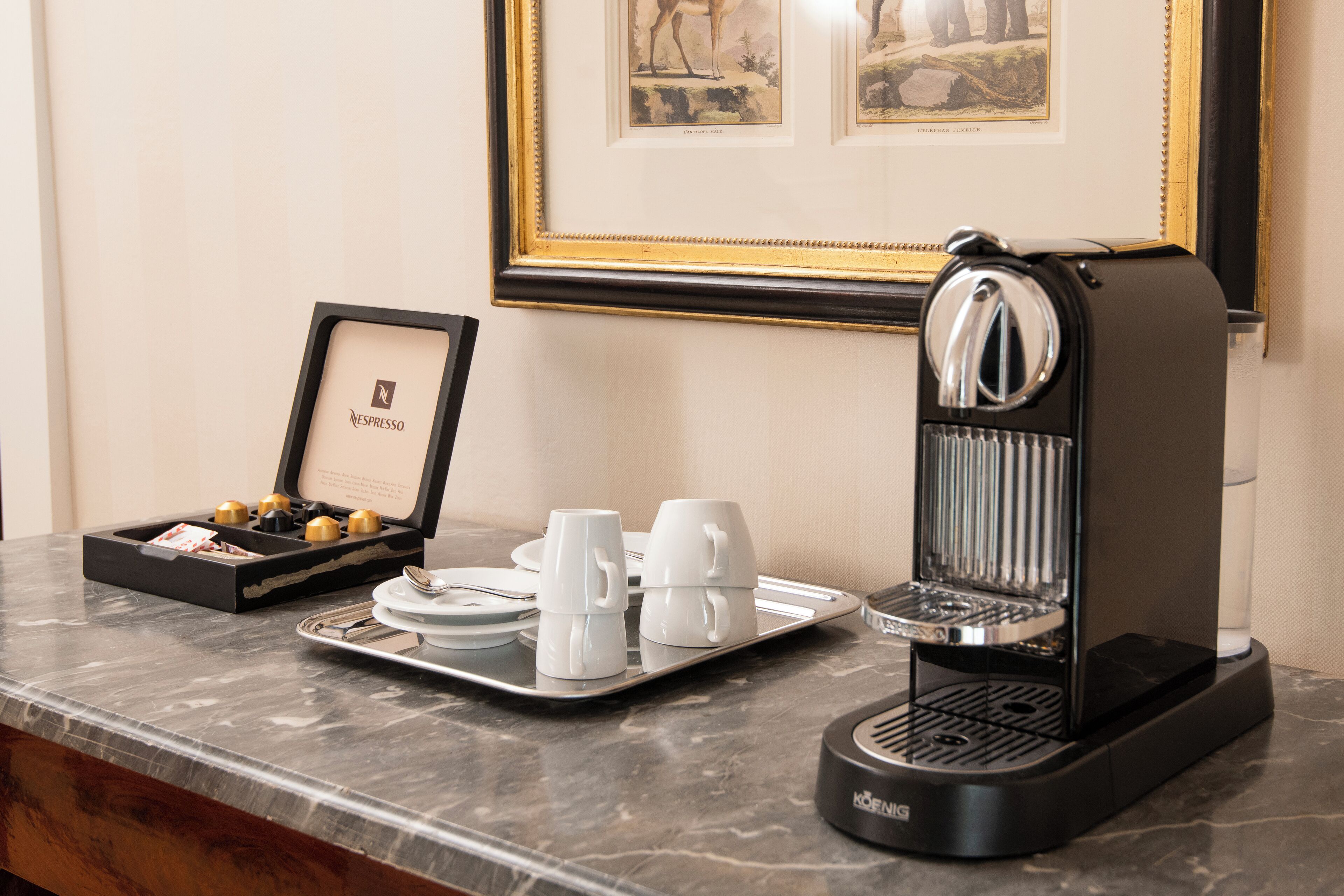 Uma máquina de café, um tabuleiro com xícaras e uma caixa de cápsulas de café em uma bancada de mármore.