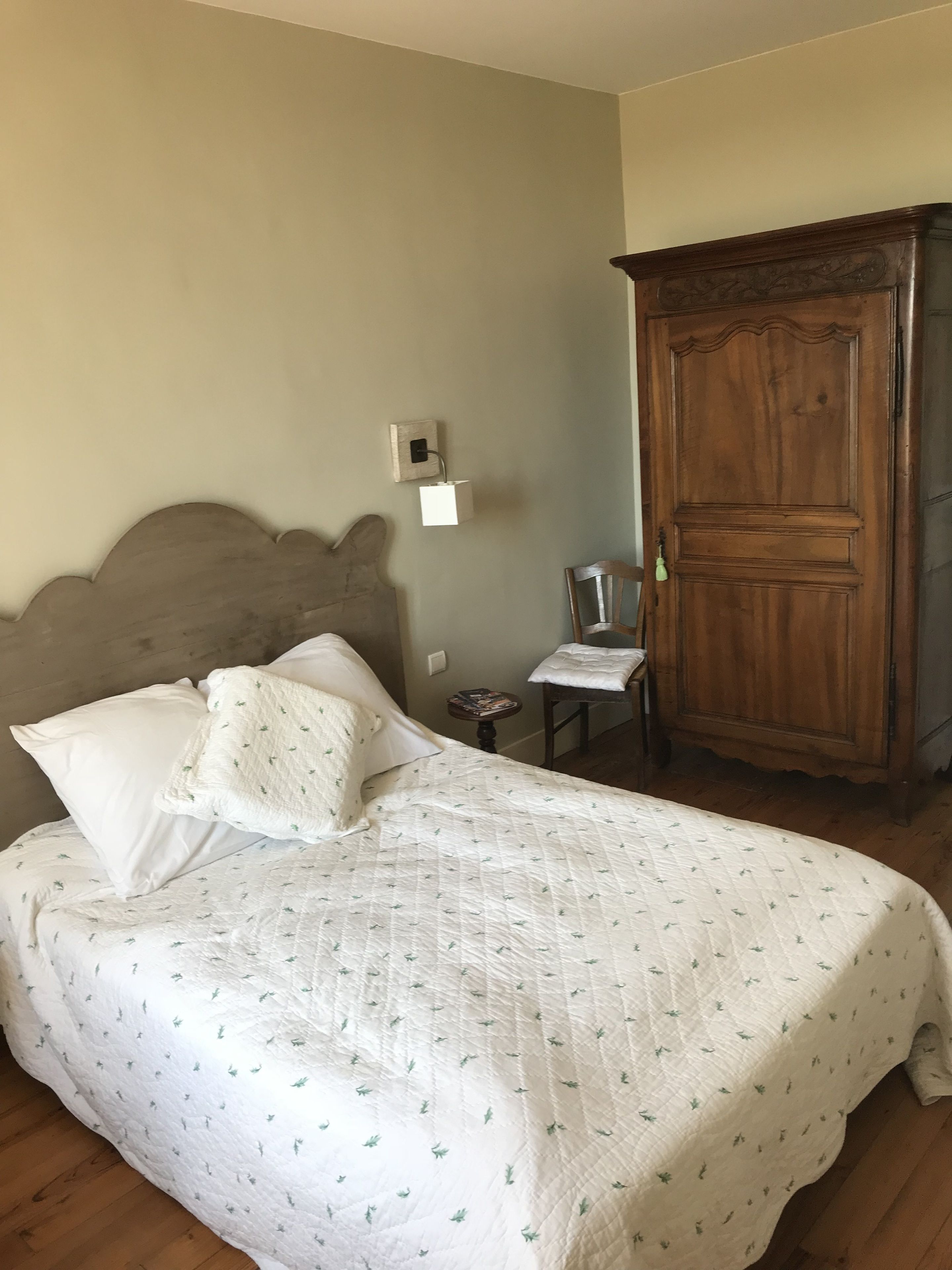 Quarto com cama, guarda-roupa de madeira, mesa pequena e luminária na parede.