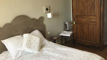 Quarto com cama, guarda-roupa de madeira, mesa pequena e luminária na parede.