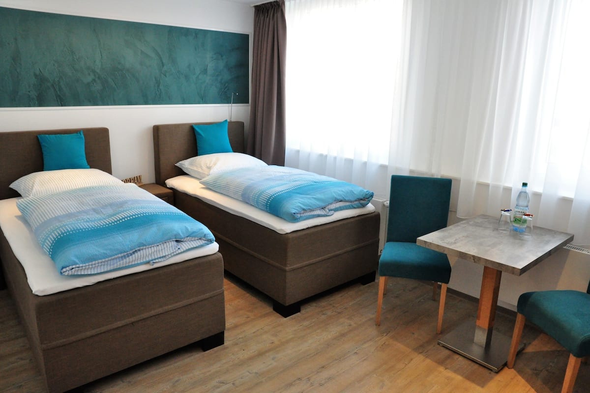 Quarto de hotel com duas camas, uma mesinha e uma cadeira.
