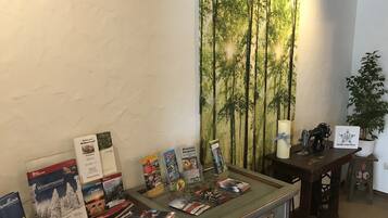 Livros e uma máquina de costura expostos sobre uma mesa de madeira num quarto com papel de parede com tema de floresta.