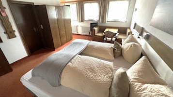 Quarto de hotel com uma cama grande, uma escrivaninha com cadeira, televisão e janela com cortinas.