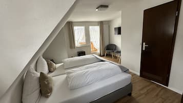 Um quarto com cama, janela com cortinas, uma cadeira e uma porta.