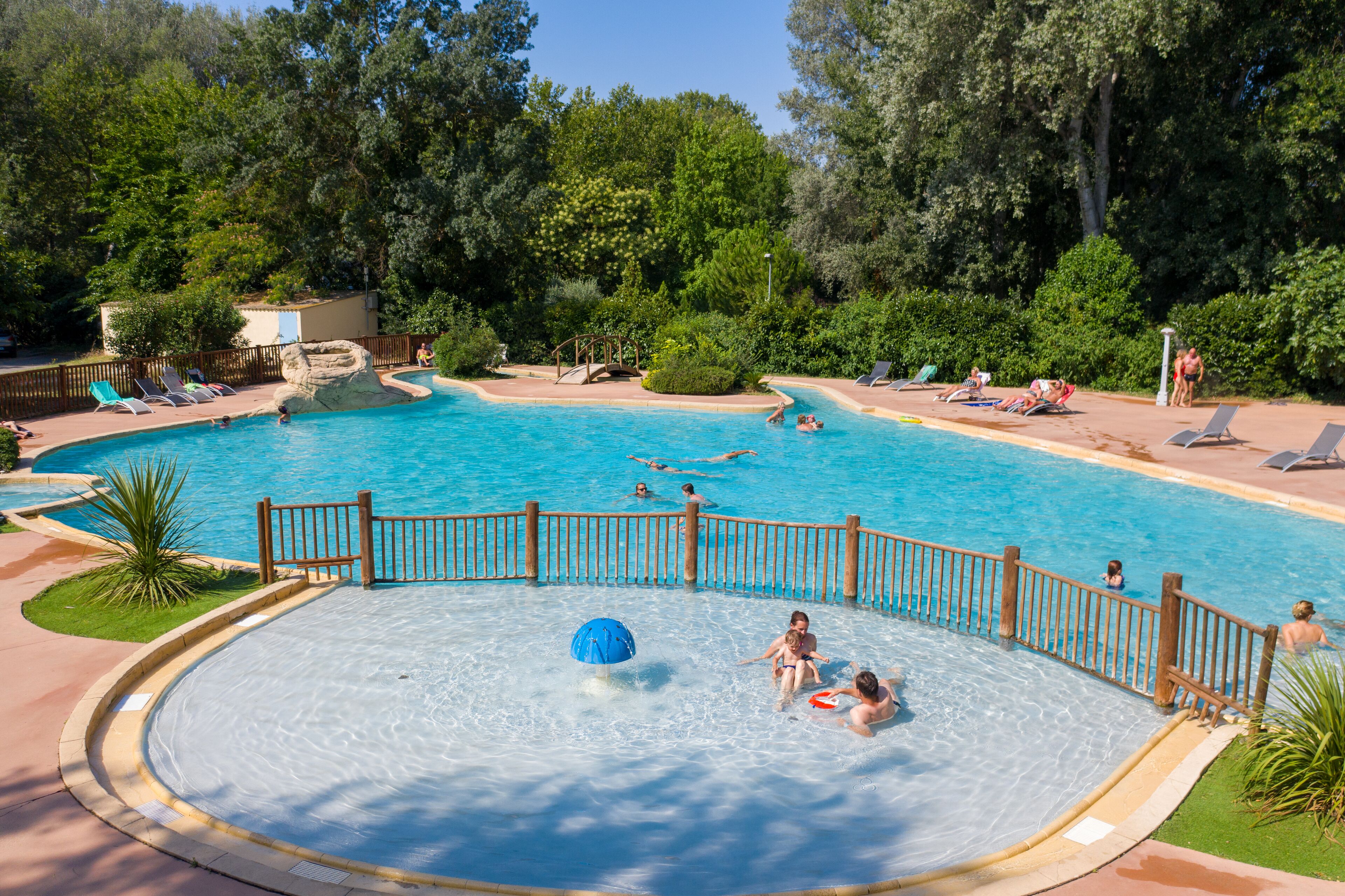 Piscina com deck de madeira, espreguiçadeiras e formação rochosa.