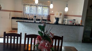 Cozinha com ilha central, armários brancos e área de refeições com mesa e cadeiras.