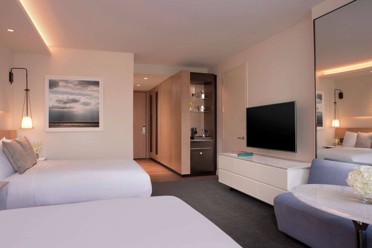 Quarto de hotel com duas camas, televisão, escrivaninha, espelho e vista para o céu.