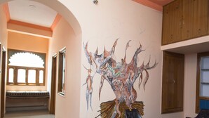 Um corredor com um mural, uma porta de madeira e uma mesa com uma placa.