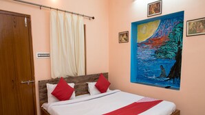 Quarto com cama de madeira, roupa de cama vermelha e branca, um quadro na parede e uma porta de madeira.