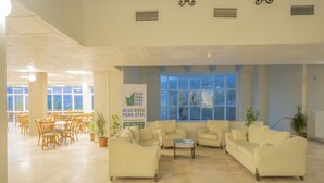 Um amplo saguão de hotel com diversas áreas de estar, incluindo sofás e cadeiras, e um espaço de refeições com mesas e cadeiras.