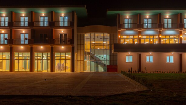 Um hotel com vários andares, fachada central de vidro, varandas e uma entrada bem iluminada.