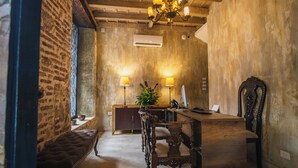 Um interior rústico com paredes de tijolos aparentes, um banco de madeira, uma escrivaninha com computador e um lustre.