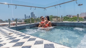 Uma piscina no terraço com guarda-corpos de vidro transparente, piso revestido e o horizonte da cidade ao fundo.
