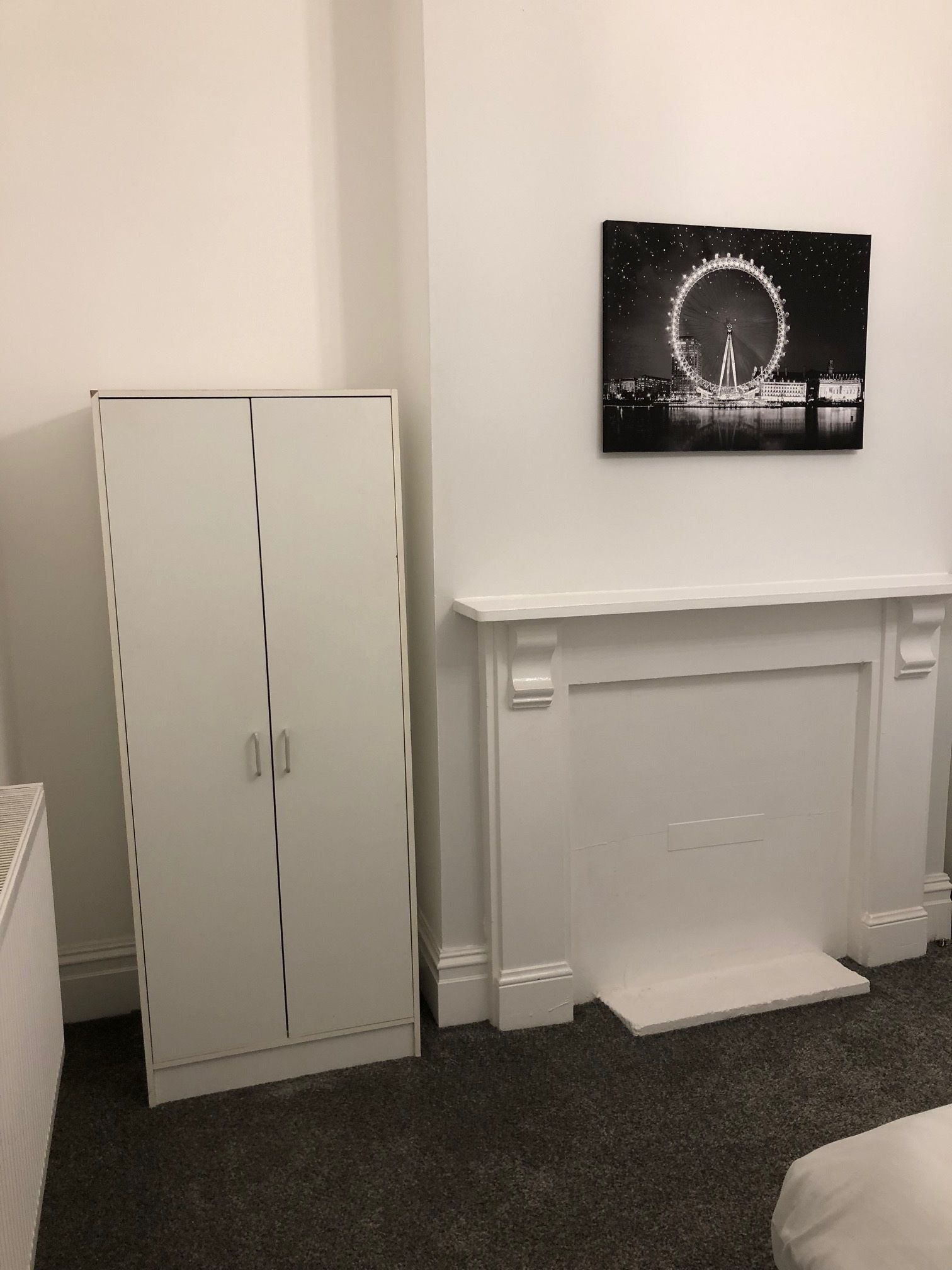 Quarto com guarda-roupa branco, lareira e quadro na parede de uma roda gigante.