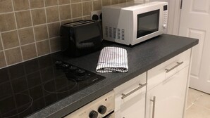 Uma cozinha com um fogão por indução preto, micro-ondas, torradeira e forno de aço inoxidável.